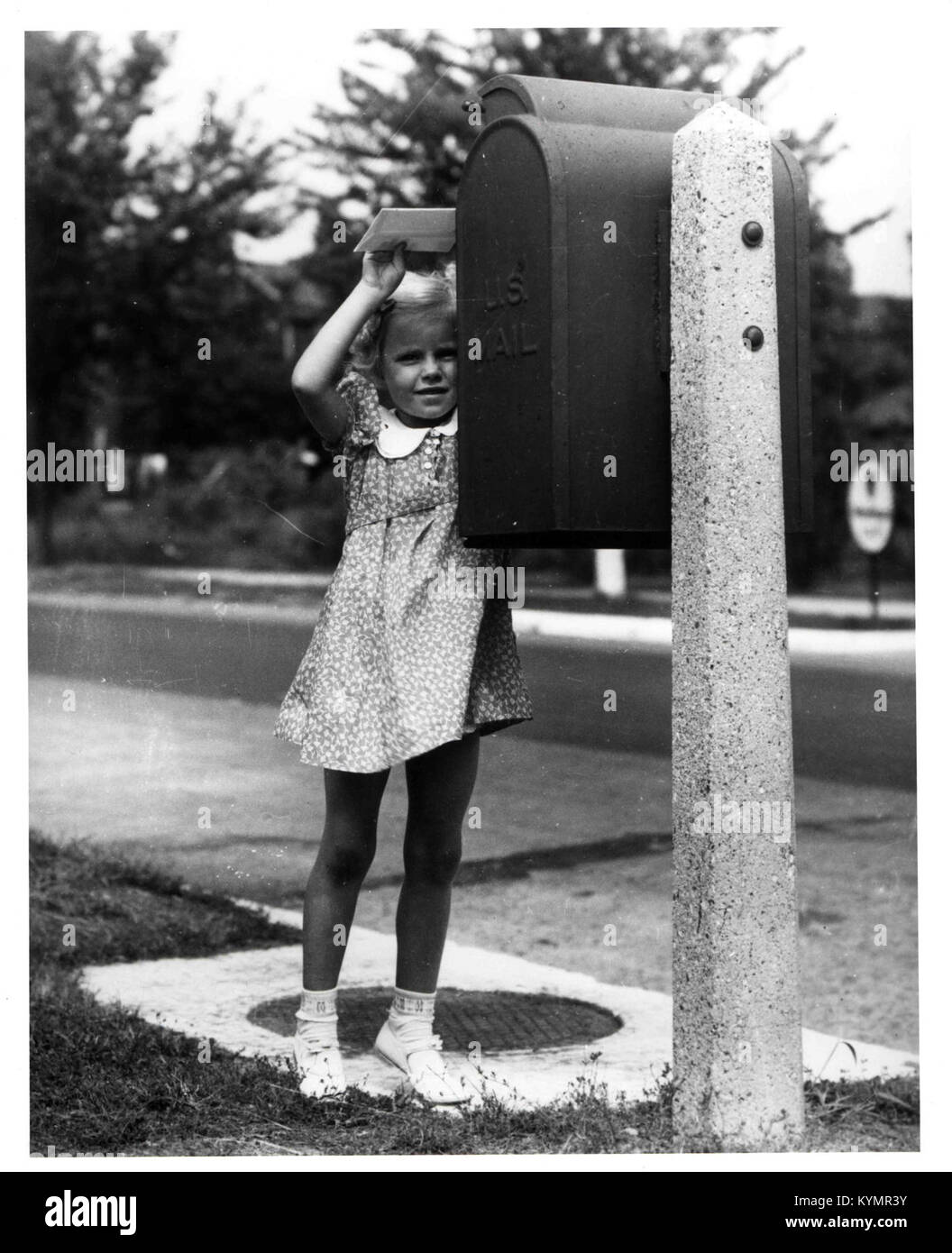 A black-and-white photograph from the 1950s showing a girl mailing a ...