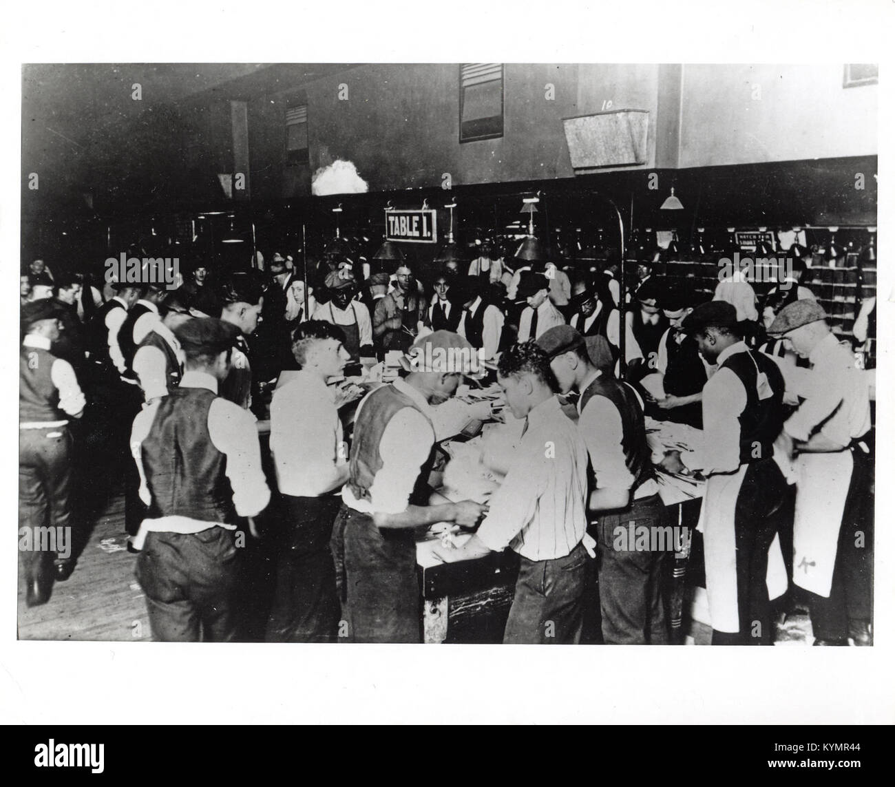 A 1930s photograph depicting postal clerks sorting mail at a busy post ...