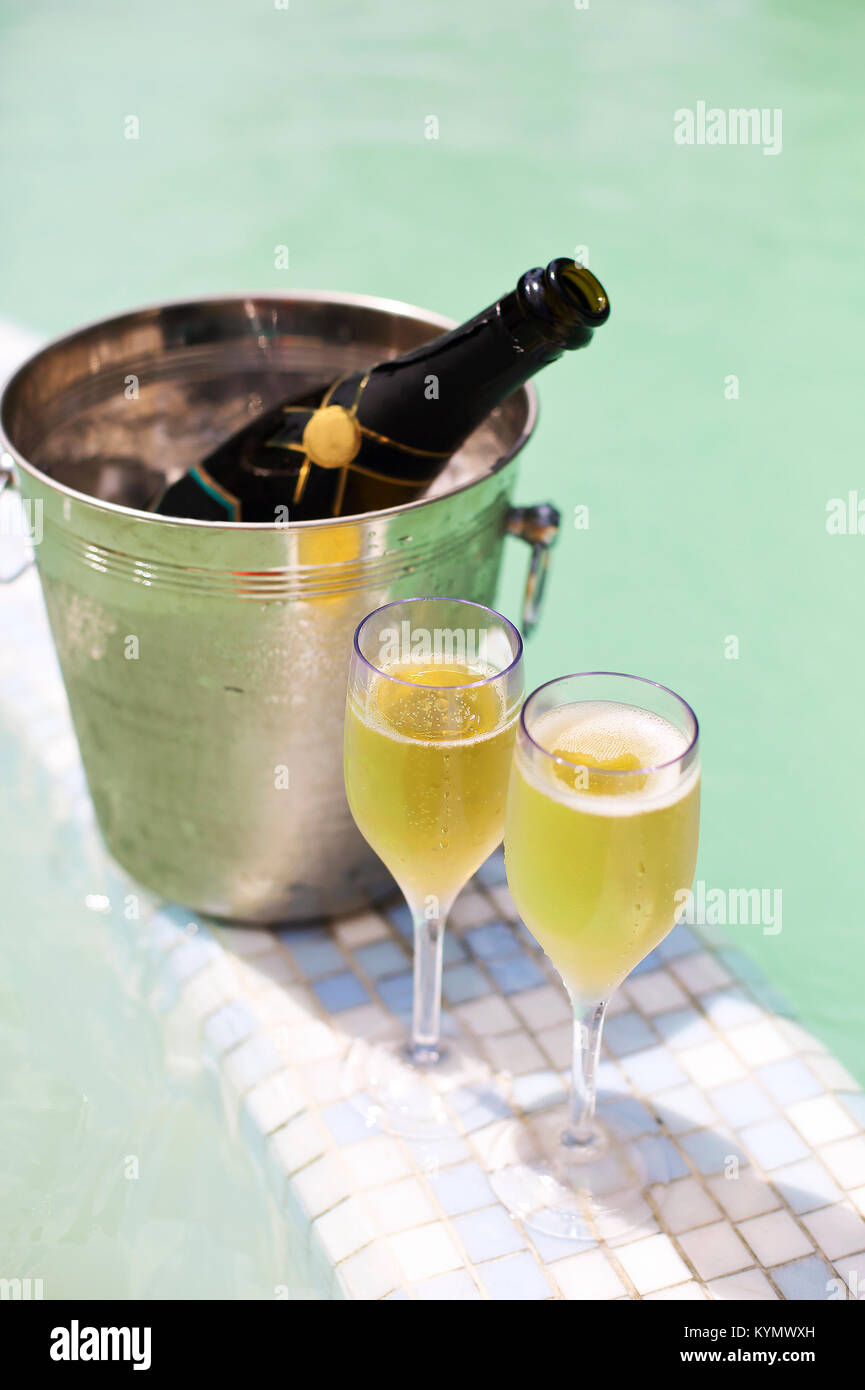Champagne glasses and bottle in ice bucket near swimming pool. Vacation ...
