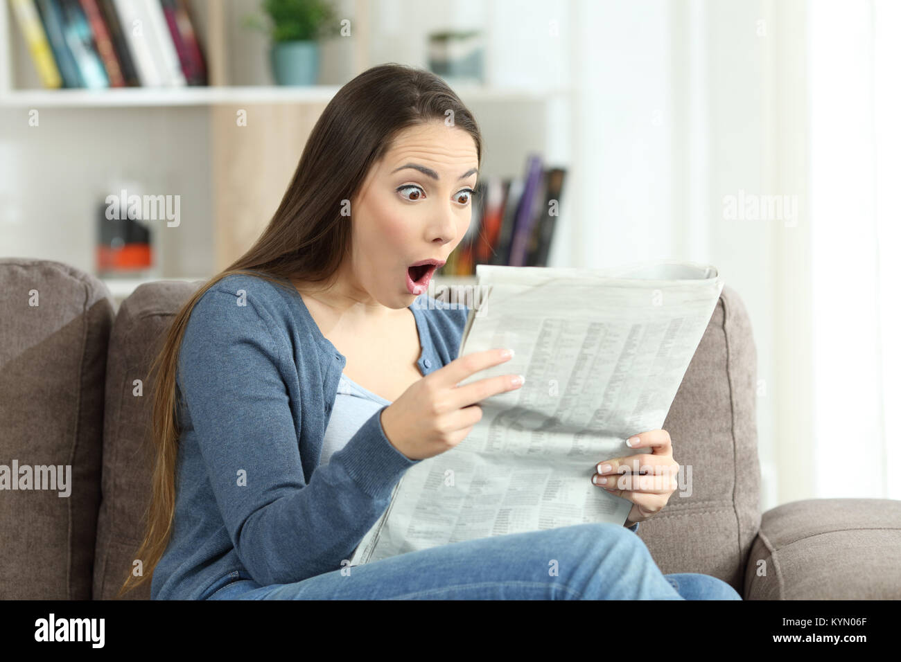 Portrait of a surprised woman reading amazing news in a newspaper ...