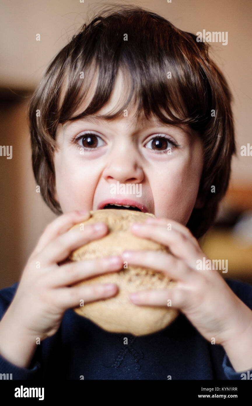 happy child eats big homemade bread, window light illuminates it Stock ...