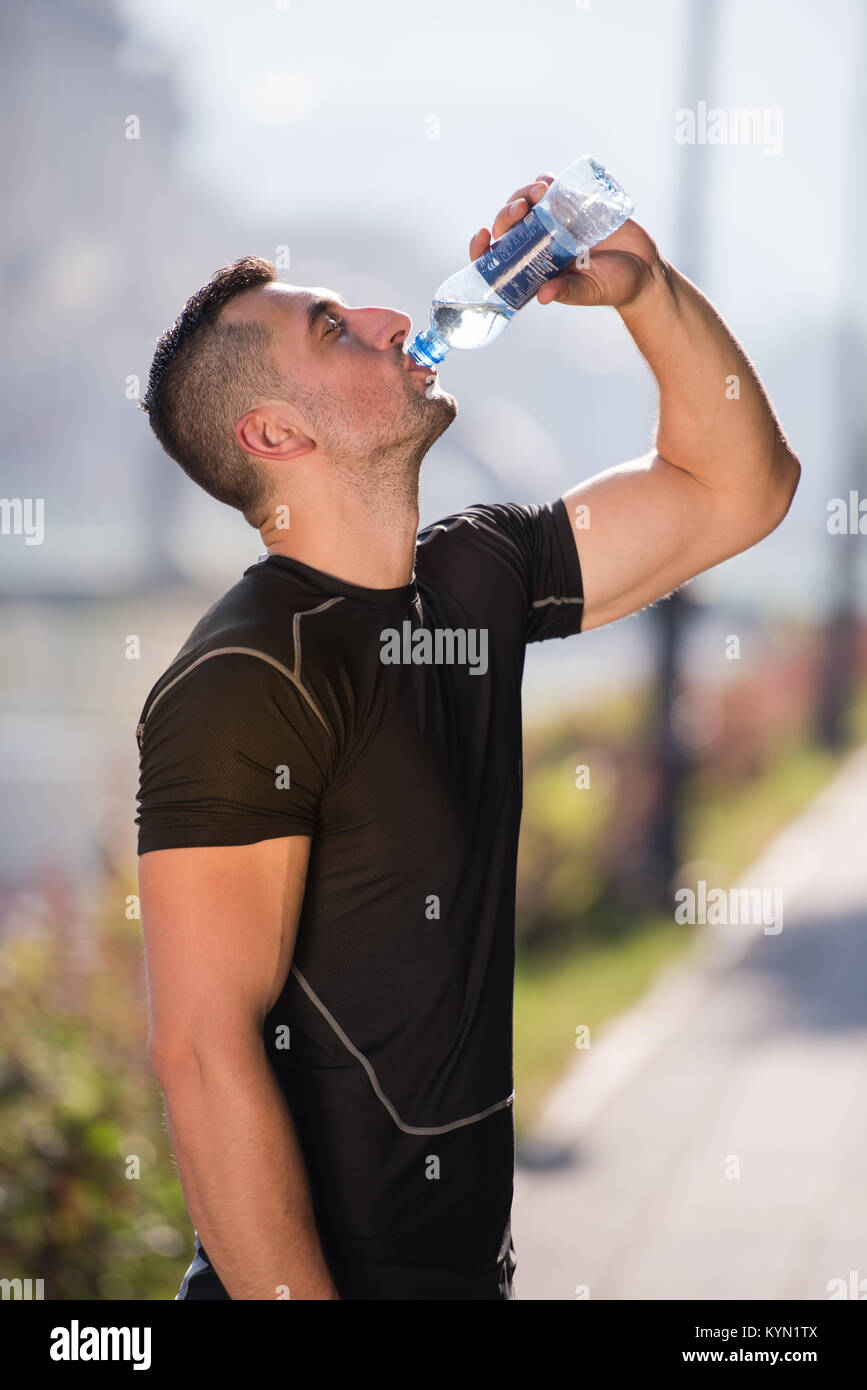 Athlete man drinking water from a bottle after jogging in the city on a ...