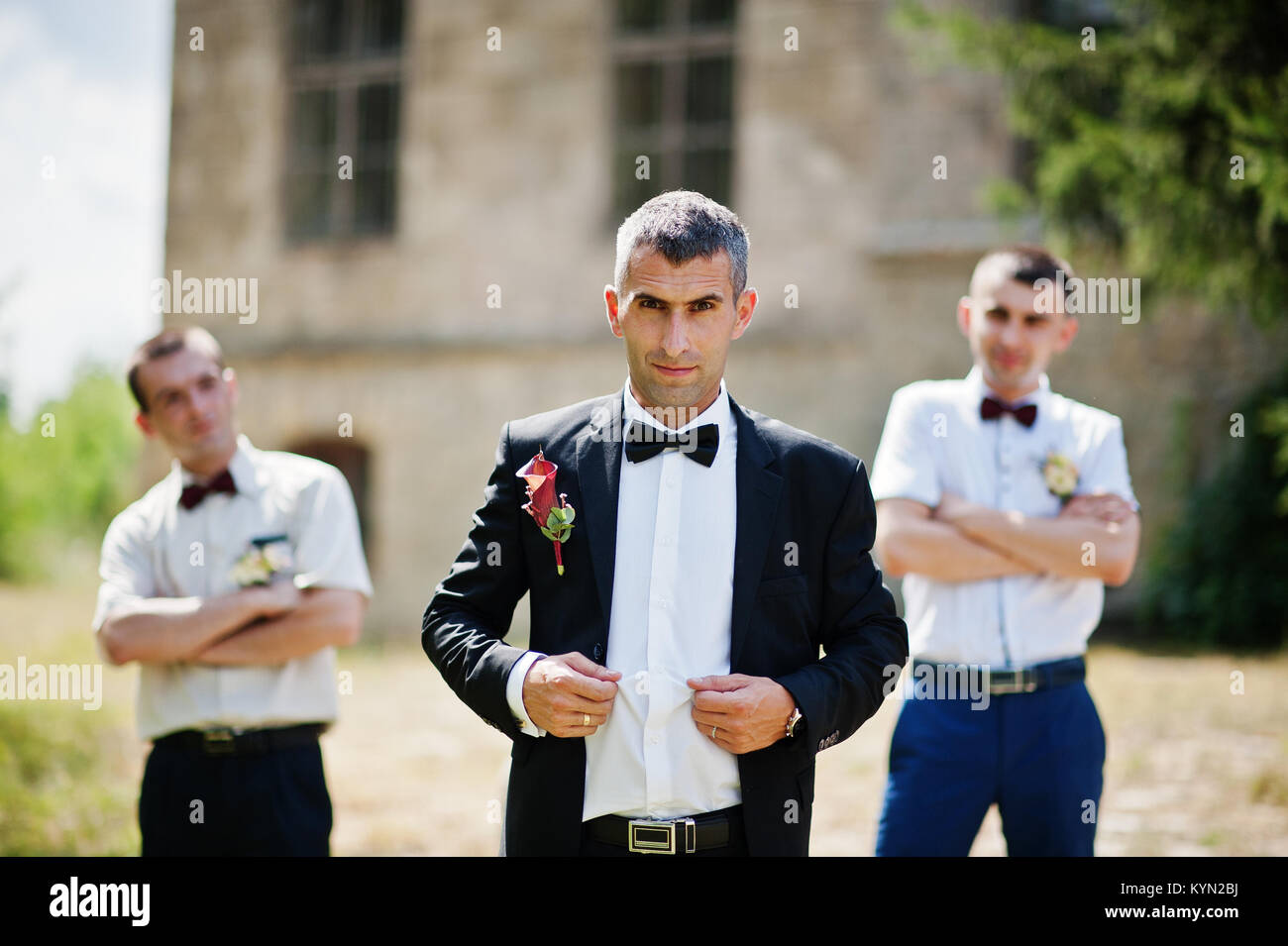 Groom posing with two groomsmen on a sunny wedding day next to the ...