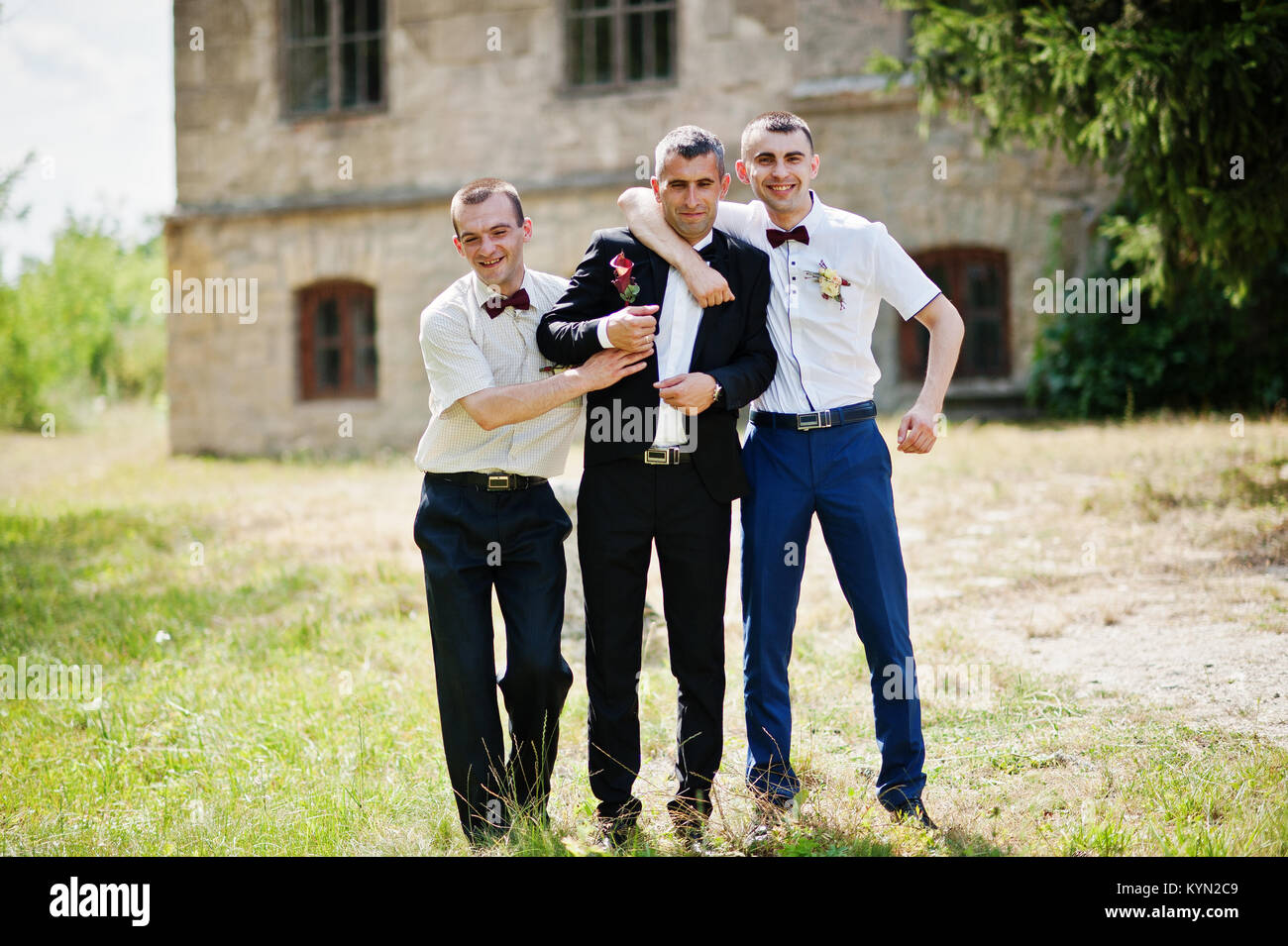 Groom posing with two groomsmen on a sunny wedding day next to the ...