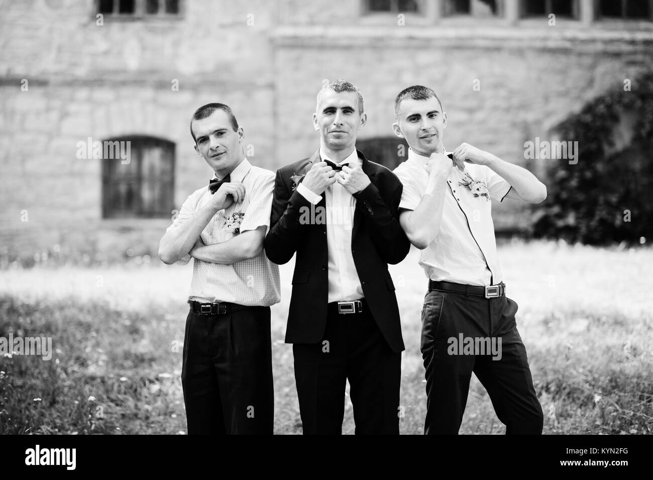 Groom posing with two groomsmen on a sunny wedding day next to the ...
