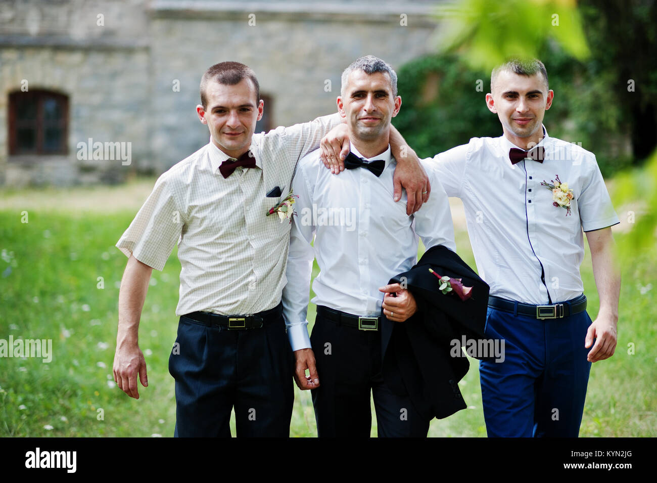 Groom posing with two groomsmen on a sunny wedding day next to the ...