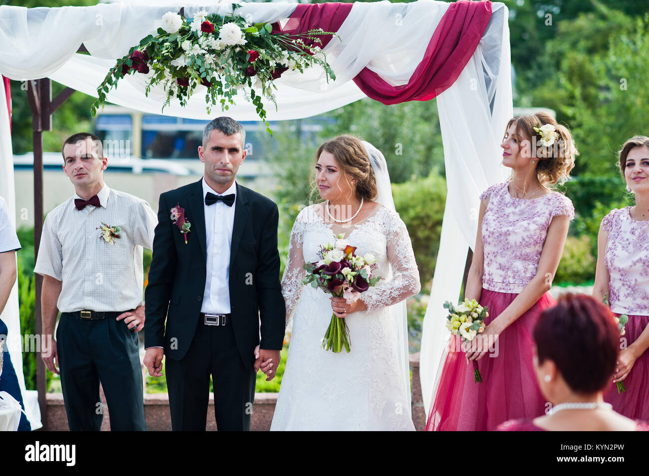 Wedding couple making vows outdoor under the floral arch in front of ...