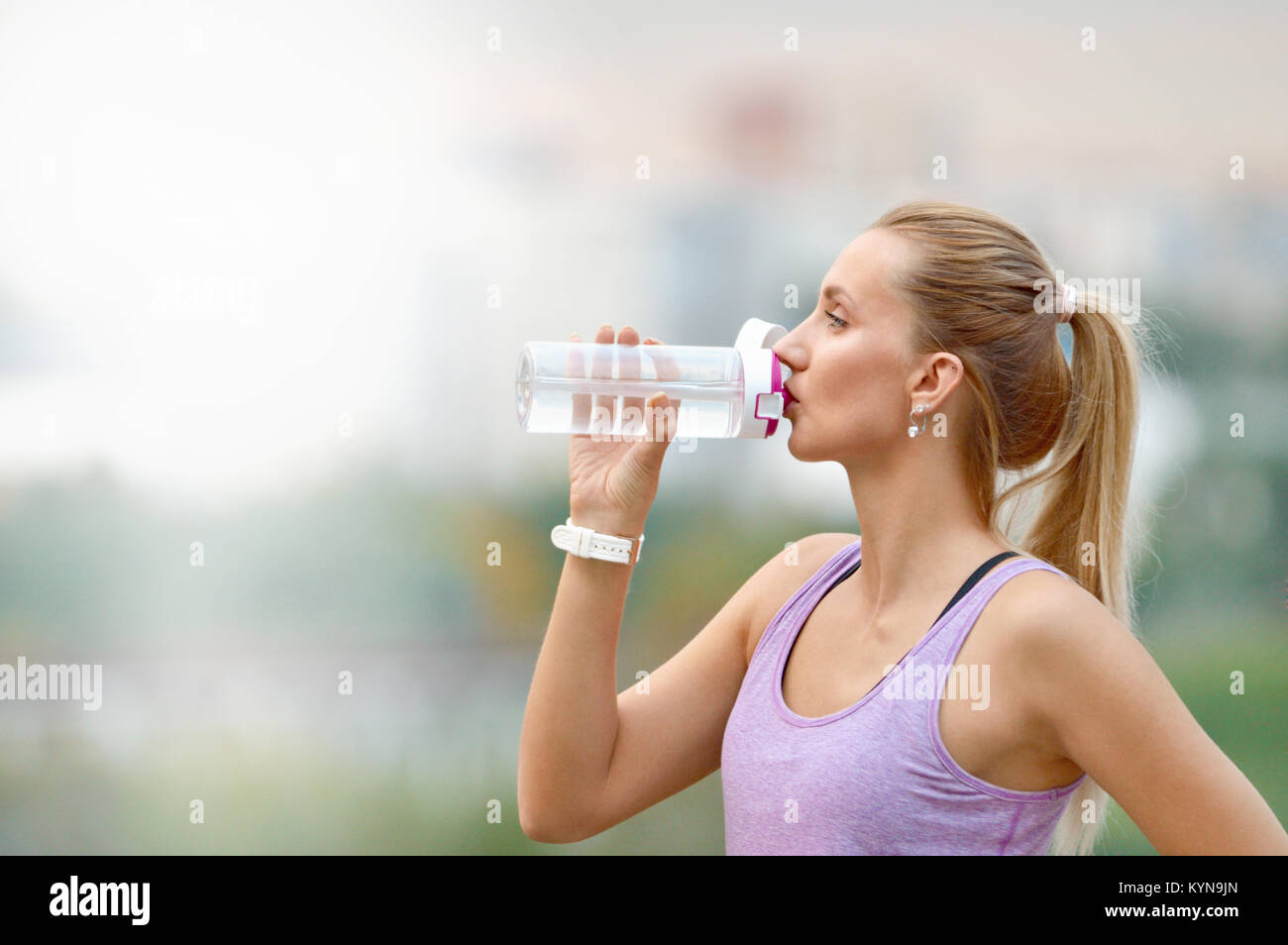 Profile portrait of sporty woman drinking in park after jogging ...