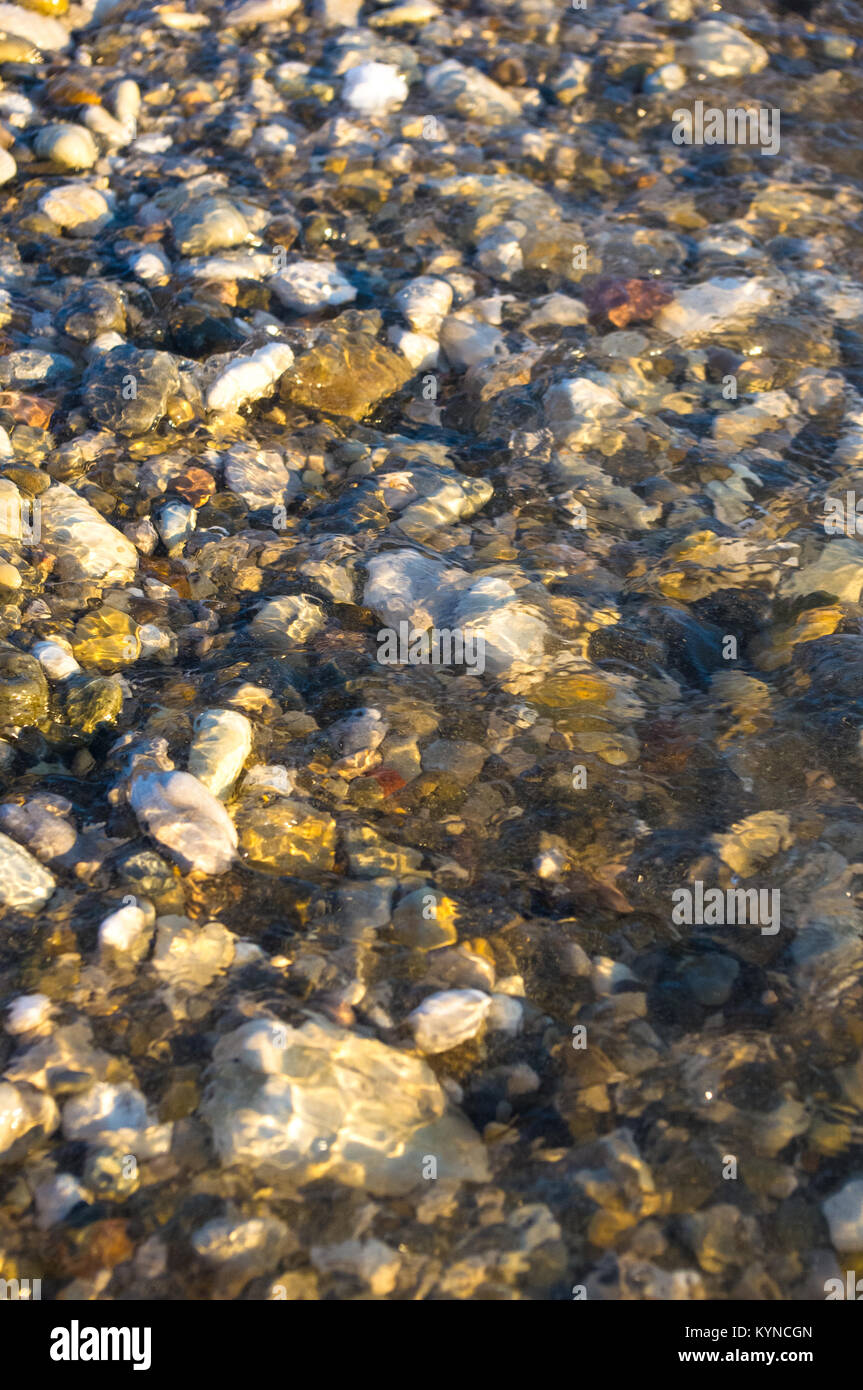 sea pebble beach with multicoloured stones, transparent waves with foam ...