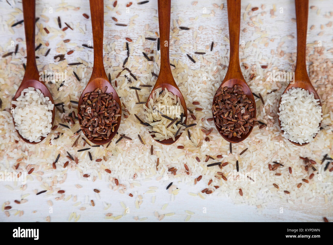Five spoons with different grades of rice on an old wooden background ...