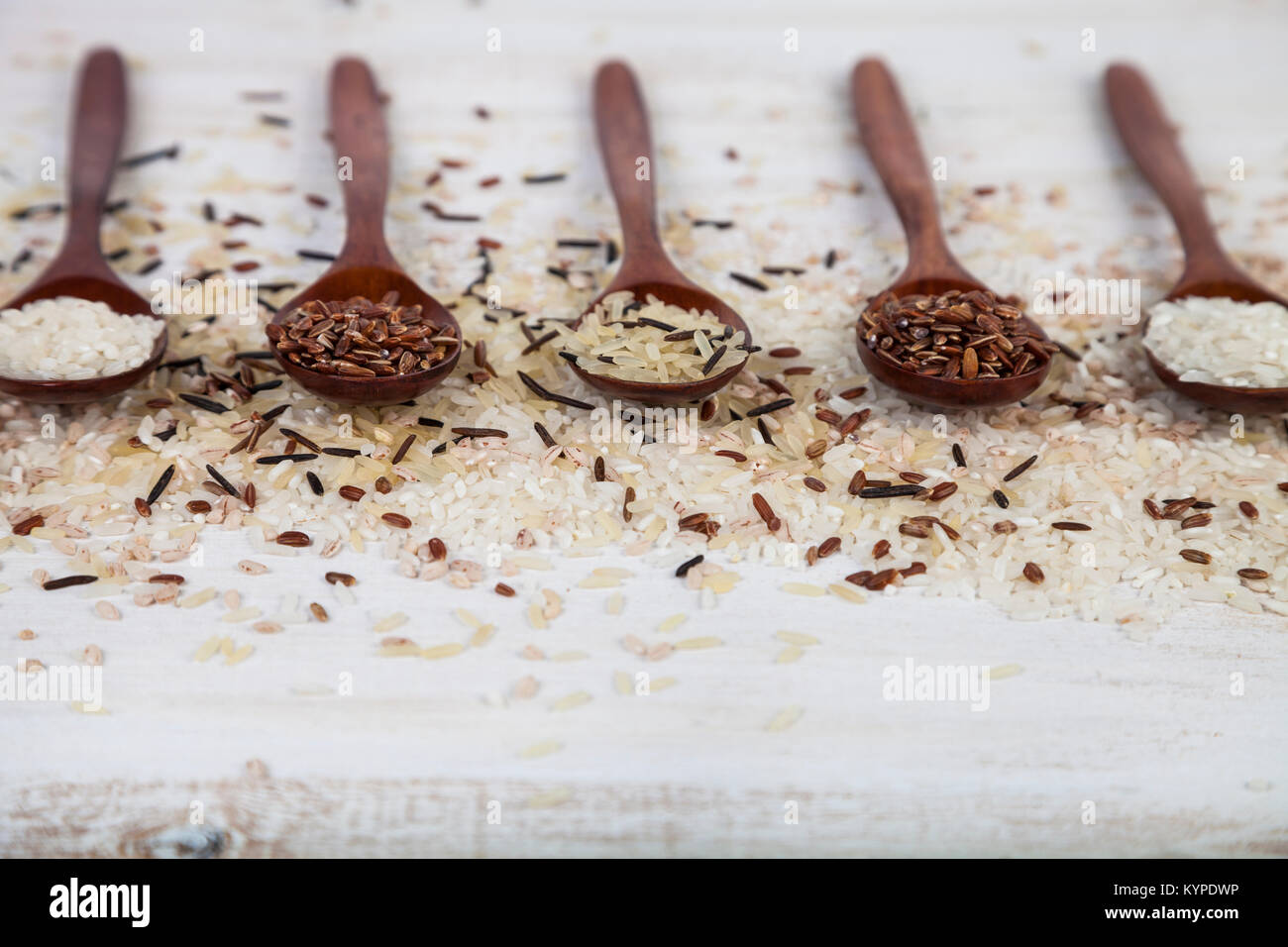 Five spoons with different grades of rice on an old wooden background ...