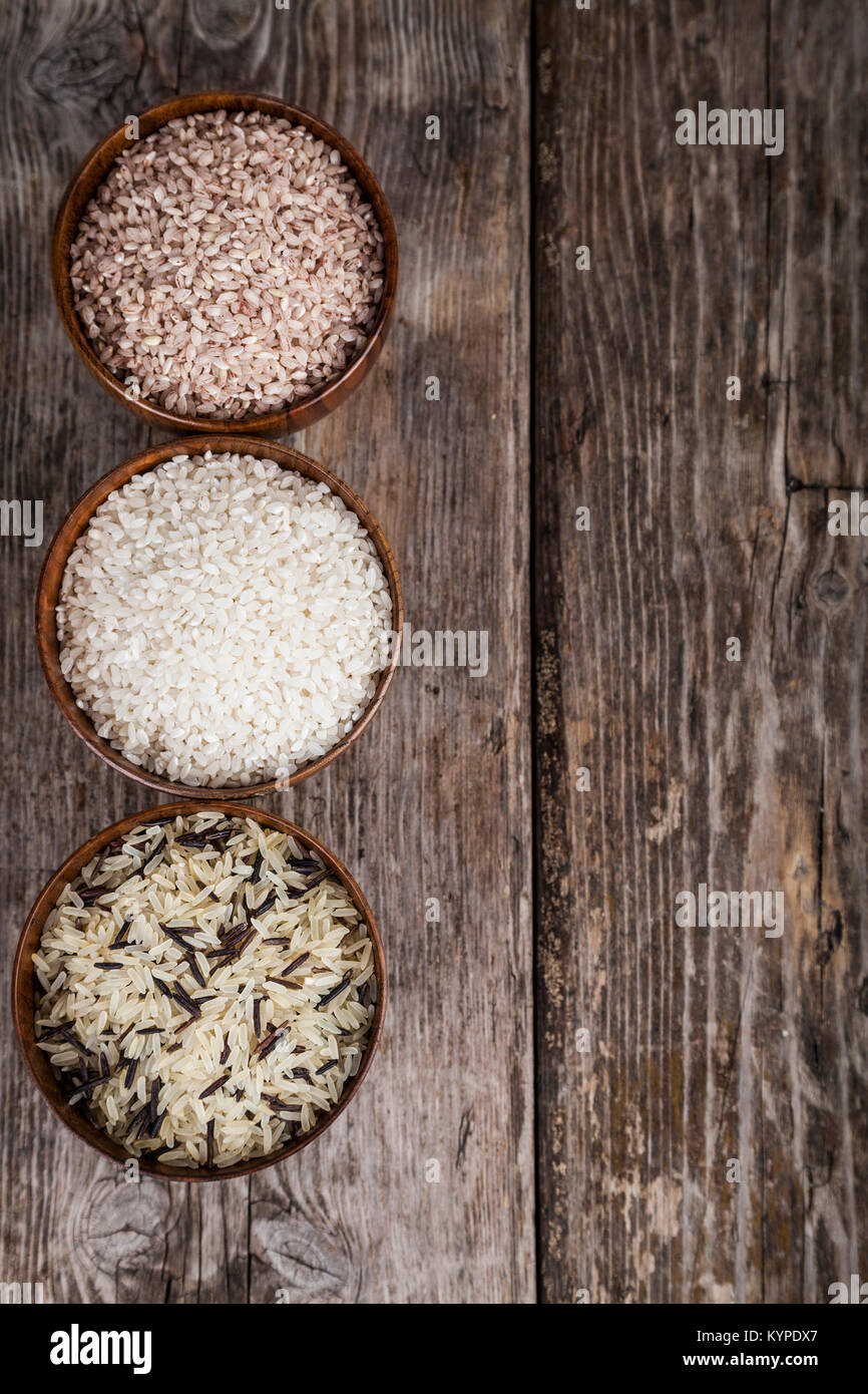 Three bowls with different varieties of rice on a wooden background ...