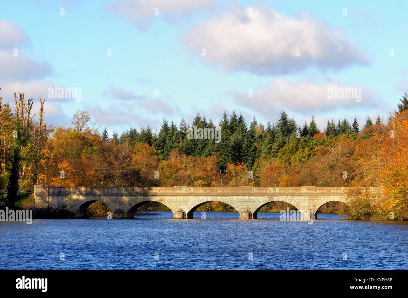 Stone bridge over a lake in the Autumn sunshine with tree leaves turned ...