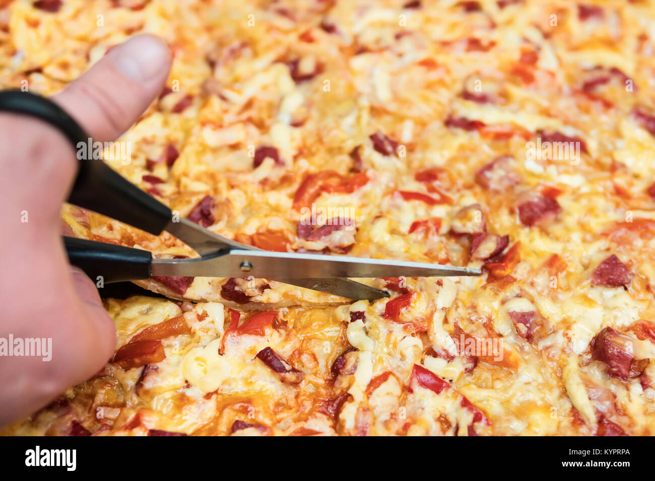 Man hand cuts a big pizza with black scissors, close-up Stock Photo - Alamy