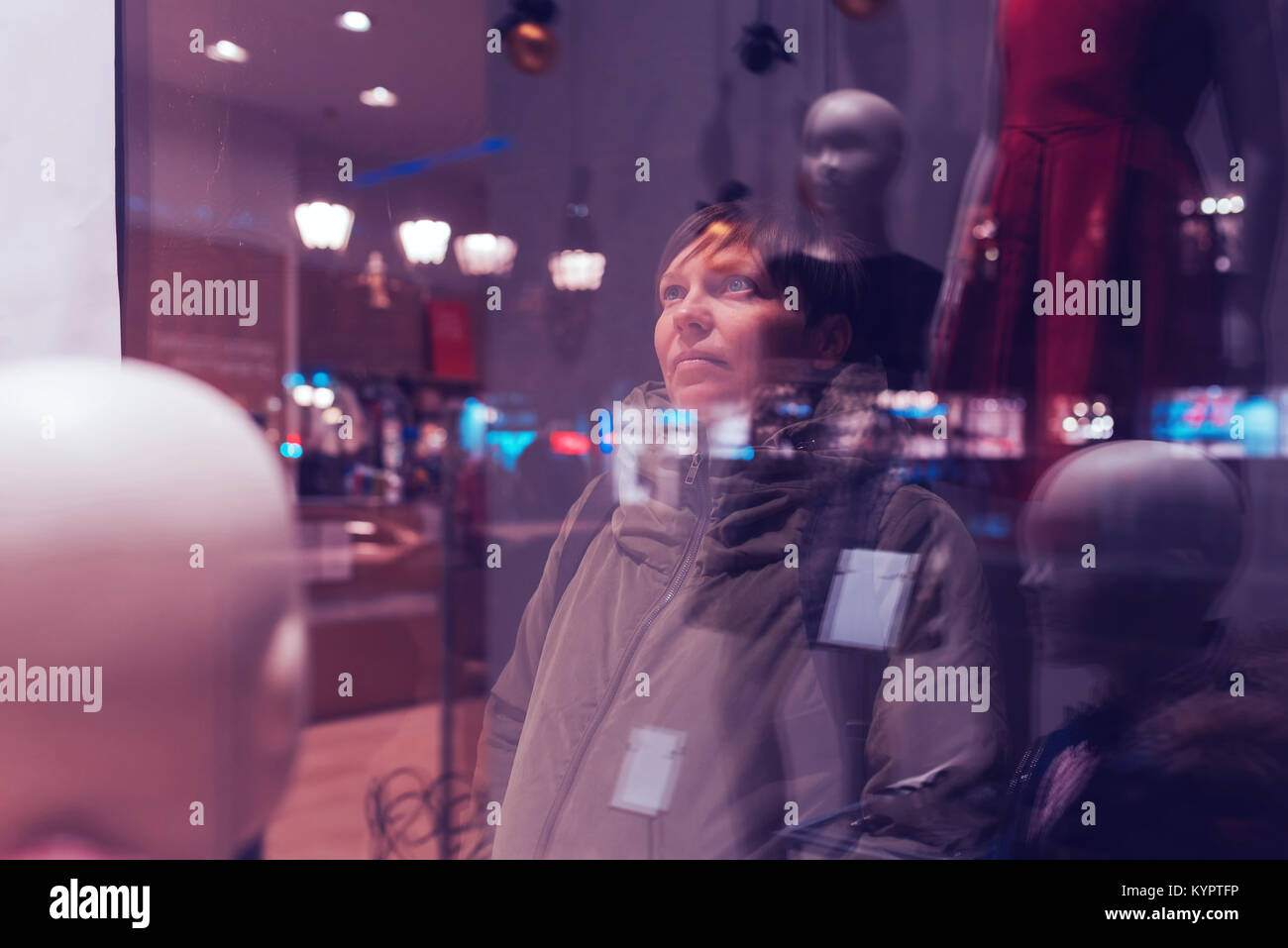 Thoughtful woman looking through shop window at night during the ...