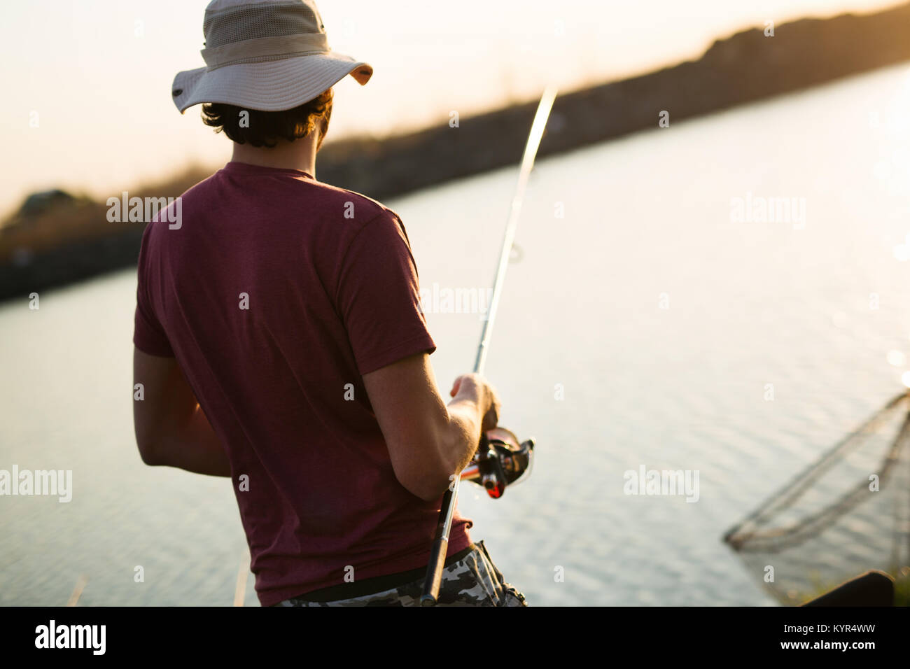 Young man fishing on lake at sunset enjoying hobby Stock Photo - Alamy