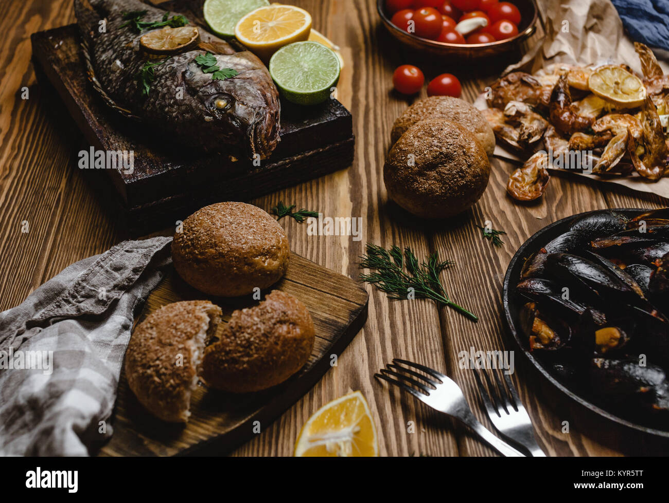 Assorted seafood and baked fish with bread and tomatoes on wooden table ...