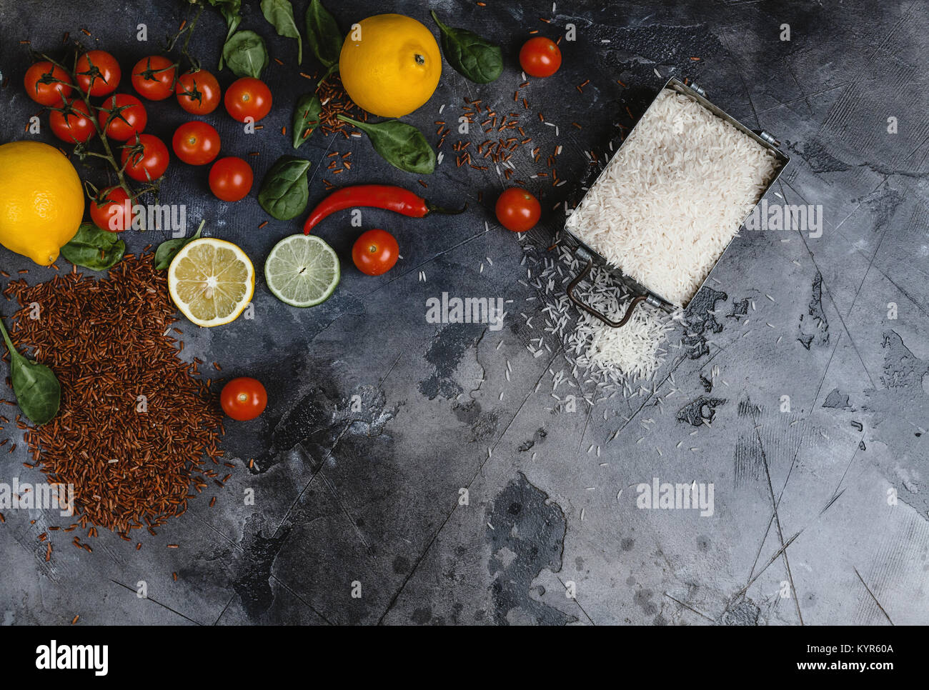top view of raw rice in container, spices and vegetables on scratched ...