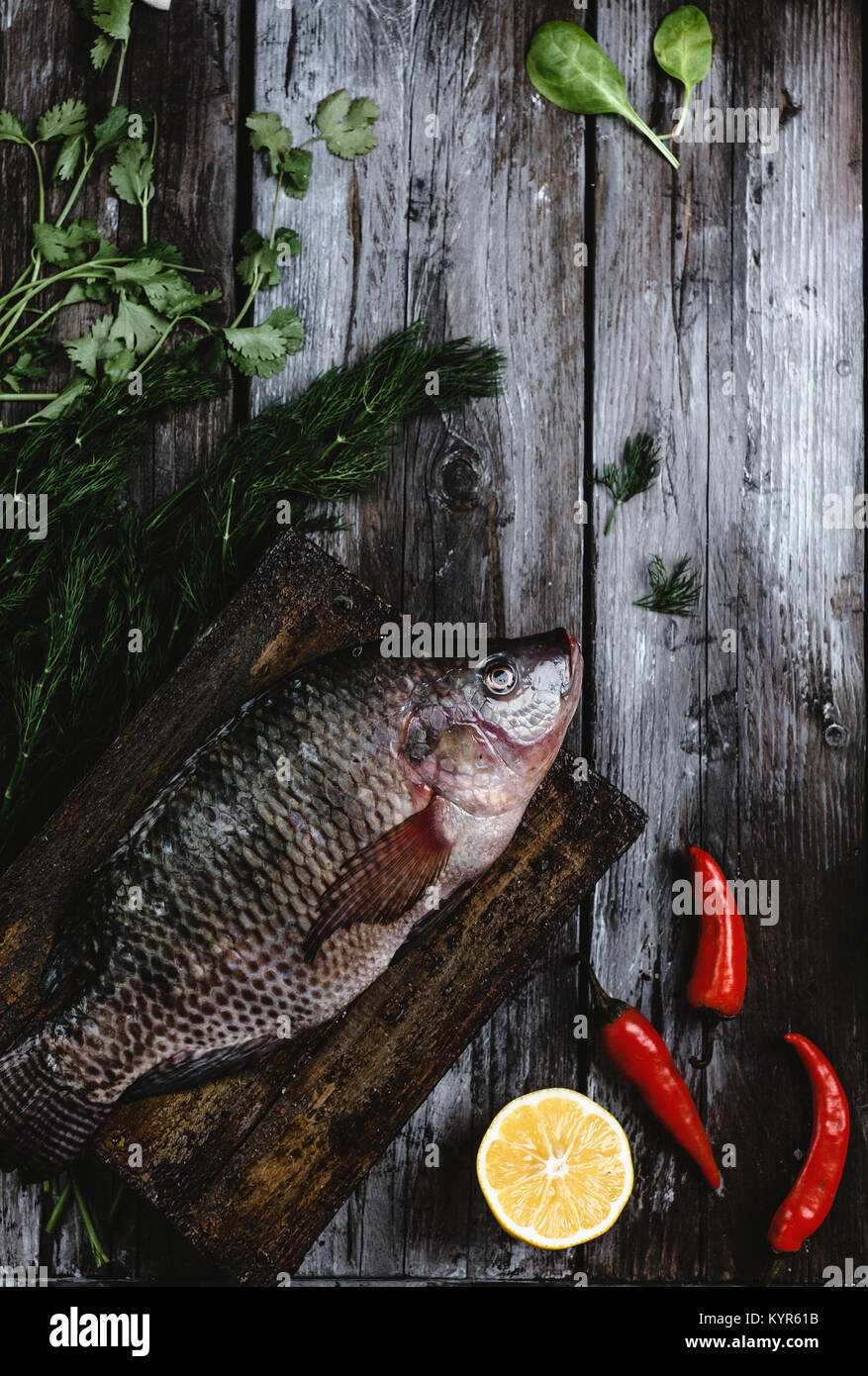 top view of fresh raw sea fish with herbs and chili peppers on rustic ...