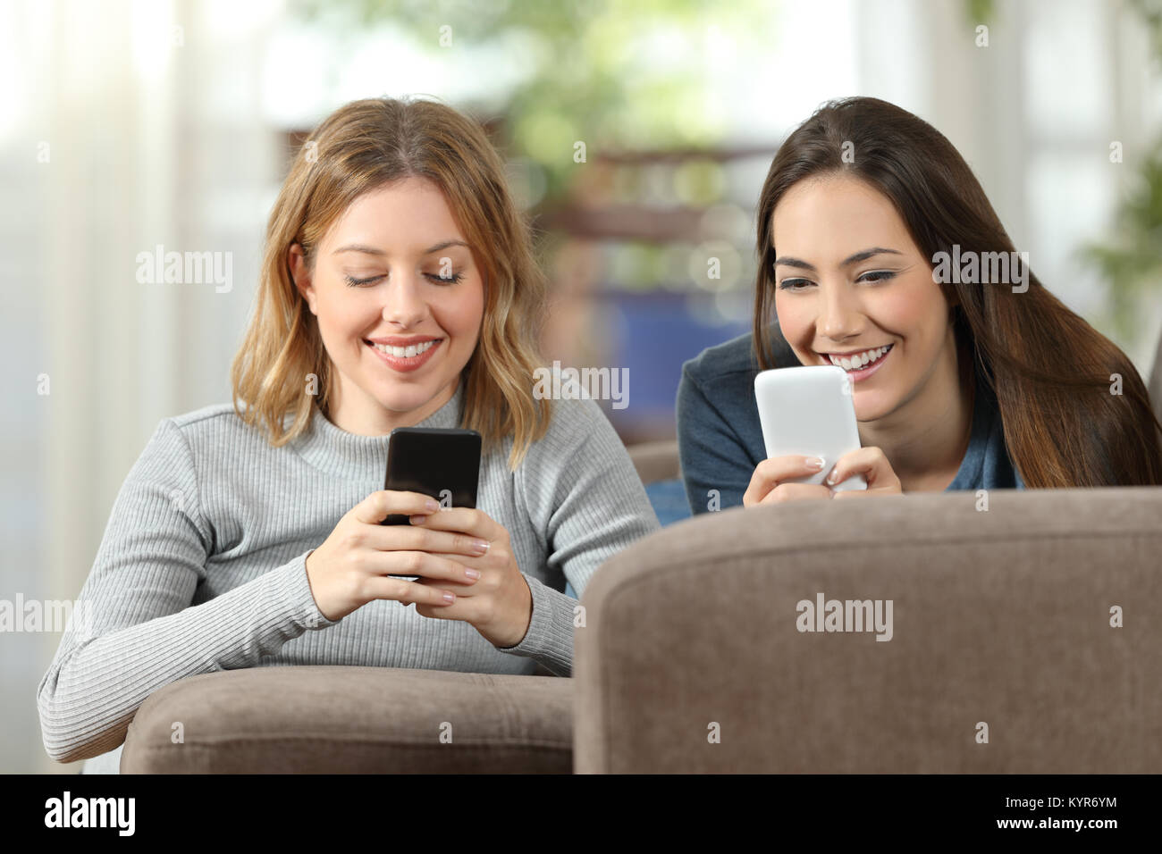 Front view of two happy roommates using two smart phones lying on a ...