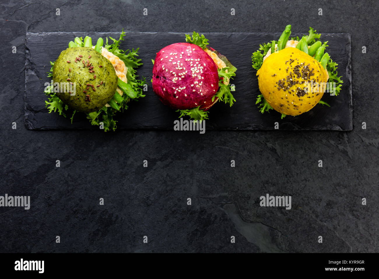 Colored green, yellow and purple burgers on slate board. Top view ...