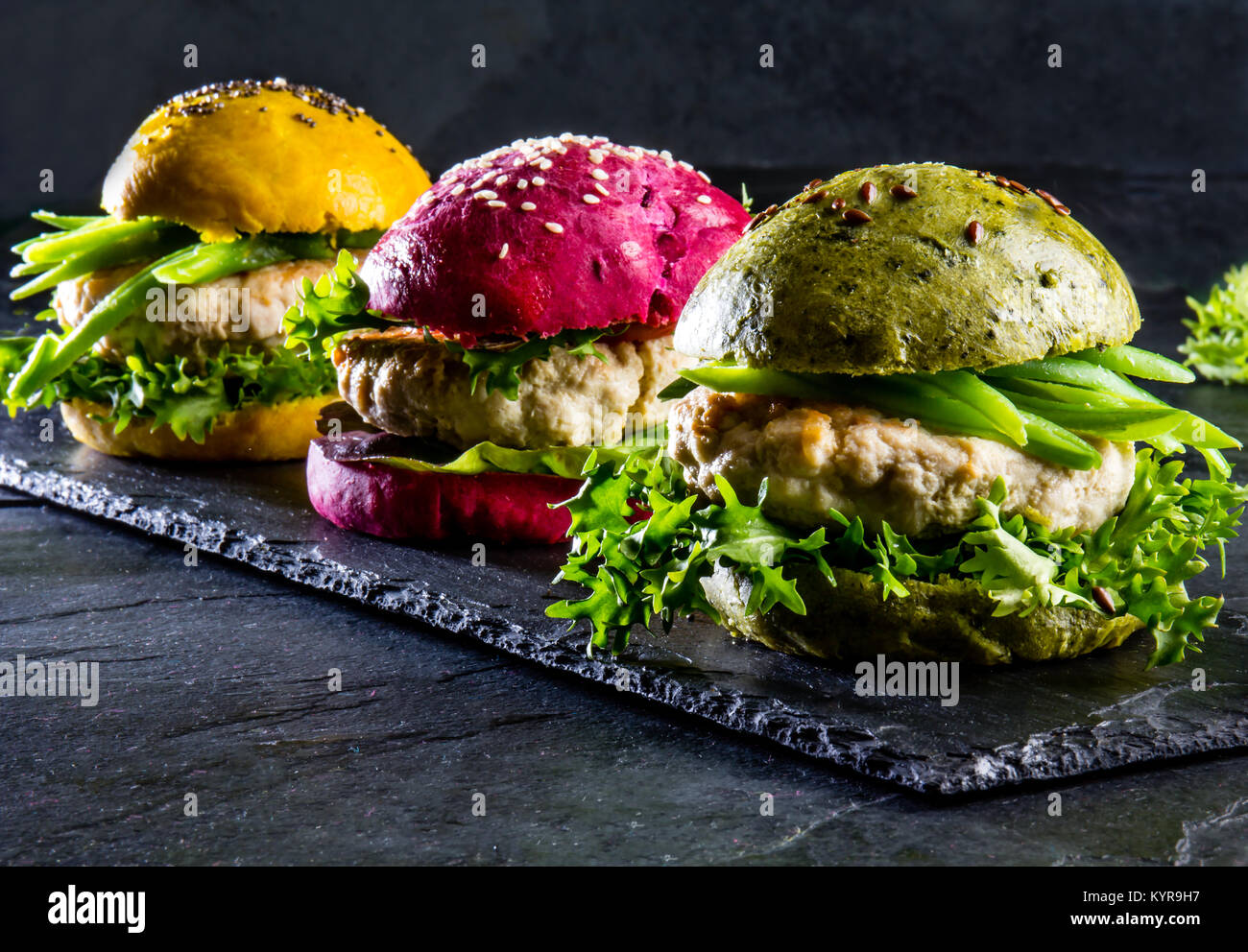 Colored green, yellow and purple burgers on slate board. Close up Stock ...
