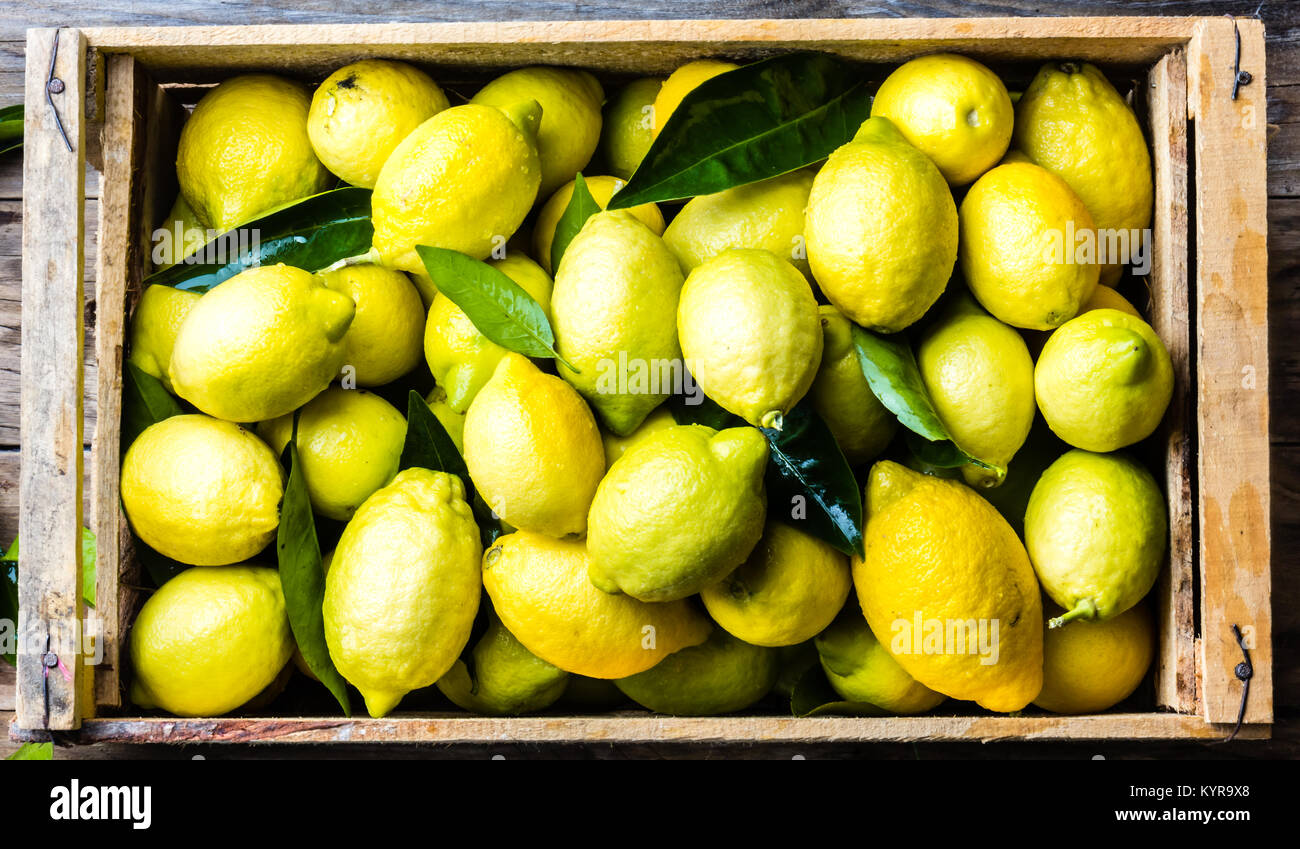 Box of yellow lemons with fresh lemon tree leaves on old wooden ...