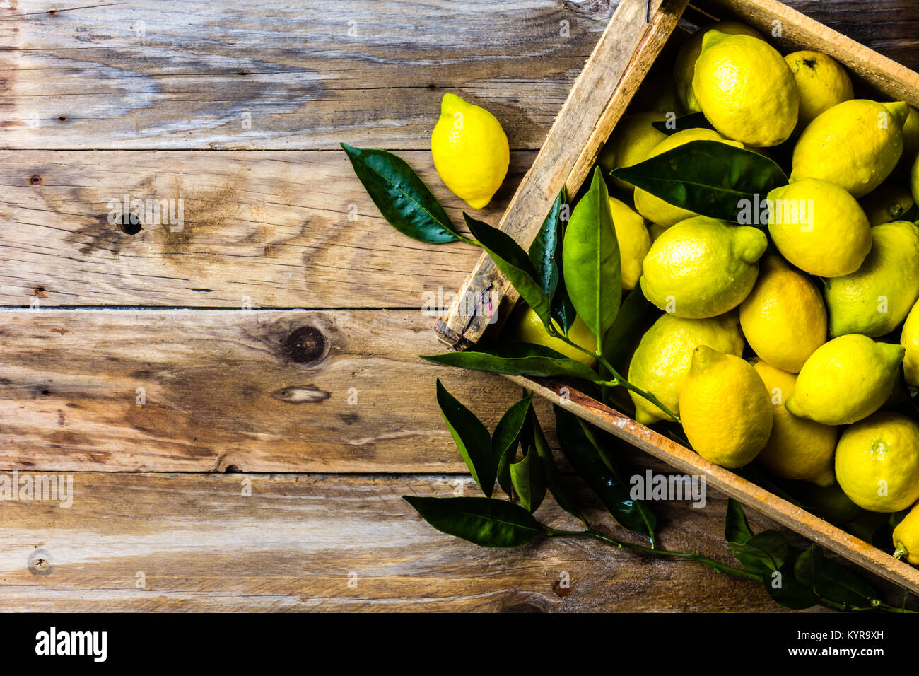 Box of yellow lemons with fresh lemon tree leaves on old wooden ...