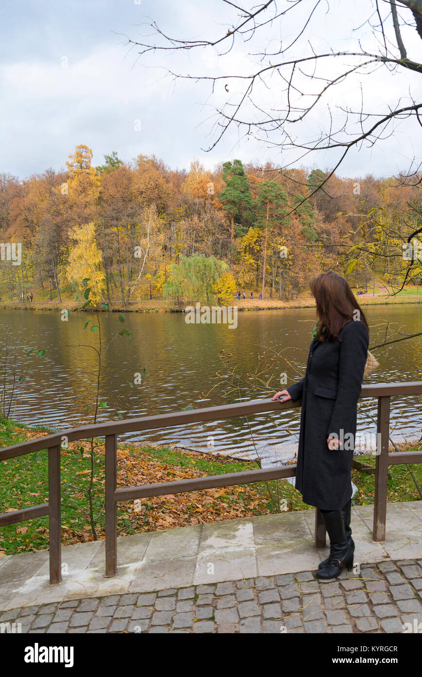 A girl stands on a bridge and looks to the opposite Bank in autumn day ...
