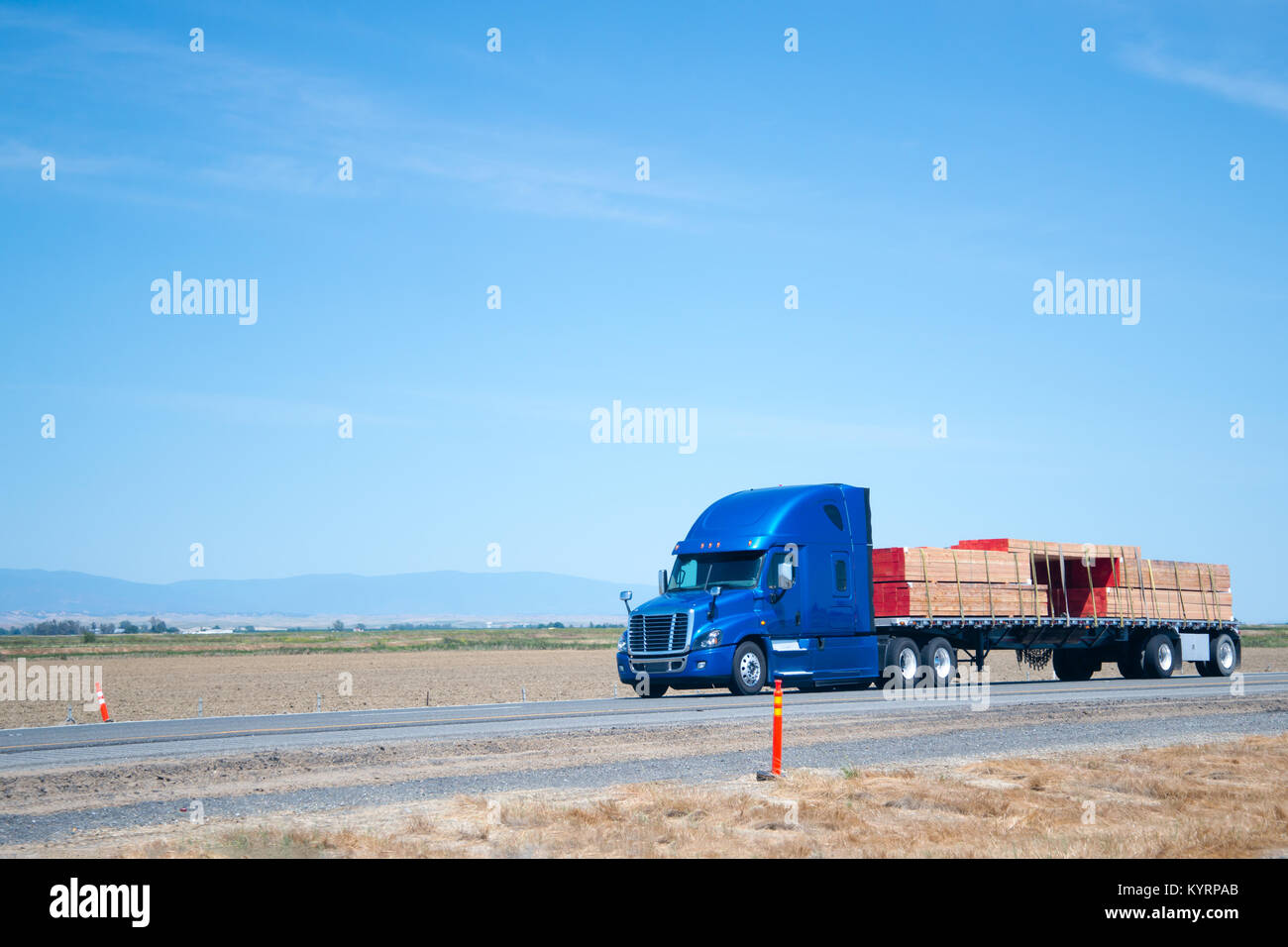 A blue modern big rig semi truck with a high cabin and a flat bad ...