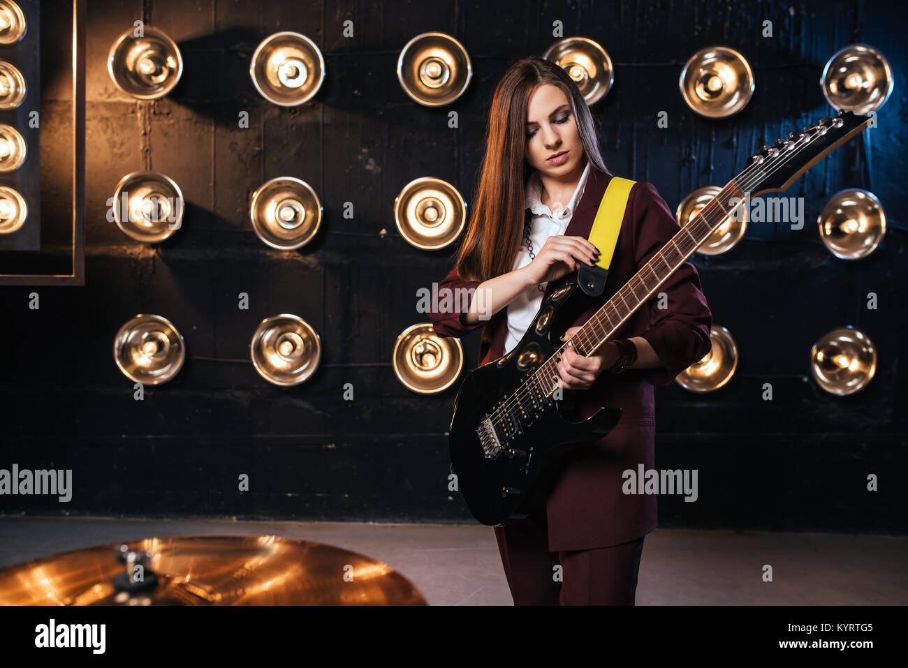 Female musician in suit playing on electric guitar, stage with lights ...