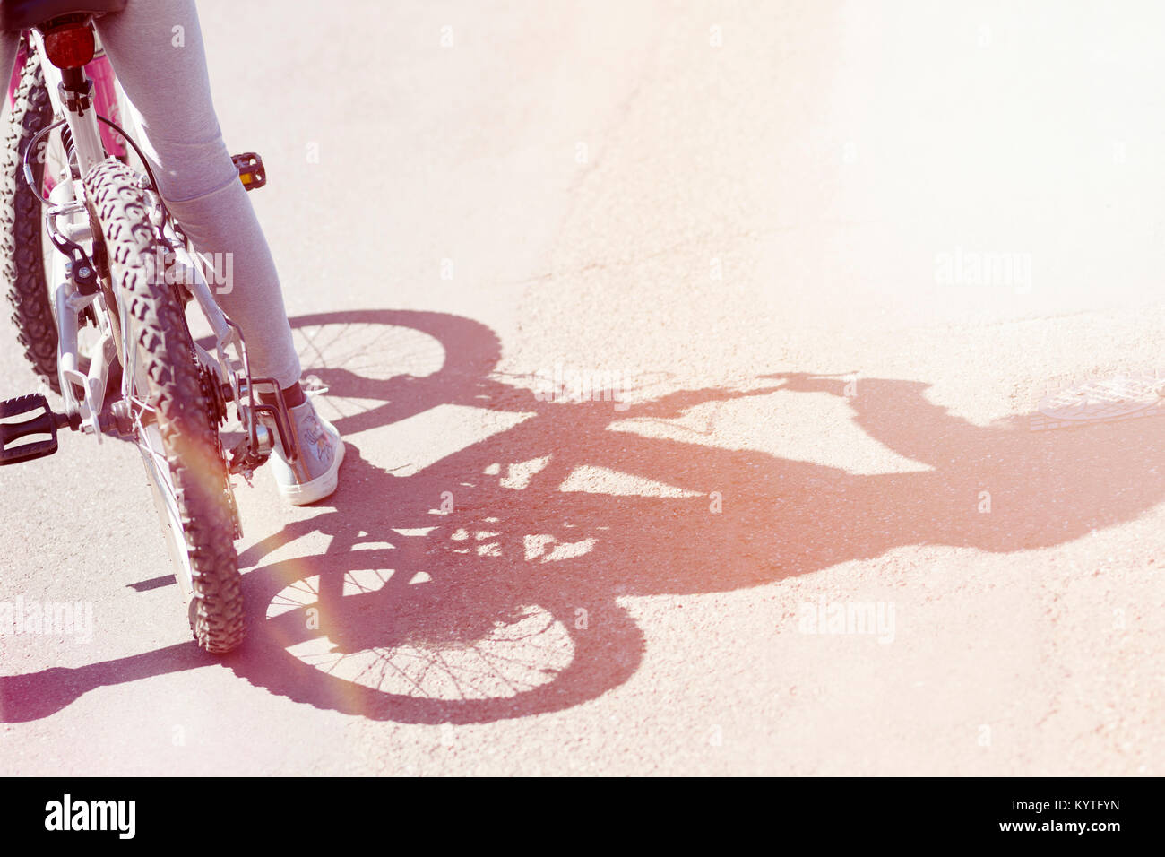 Cropped image of child on bicycle with shadow falling across road ...