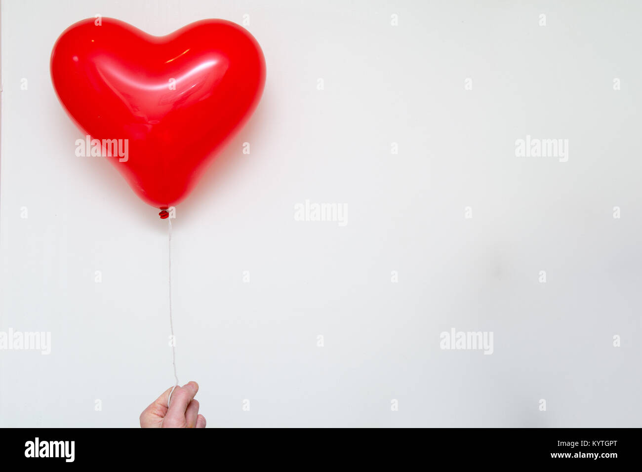 Hand holding a red heart balloon on a white background Stock Photo - Alamy