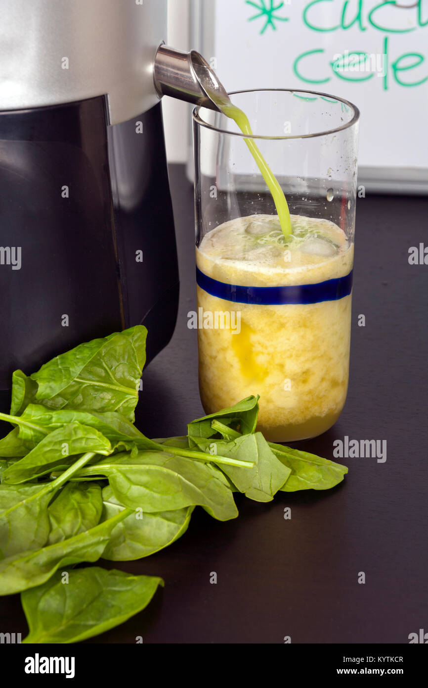 A juicer pouring fruit and vegetable juice into a drinking glass on a ...