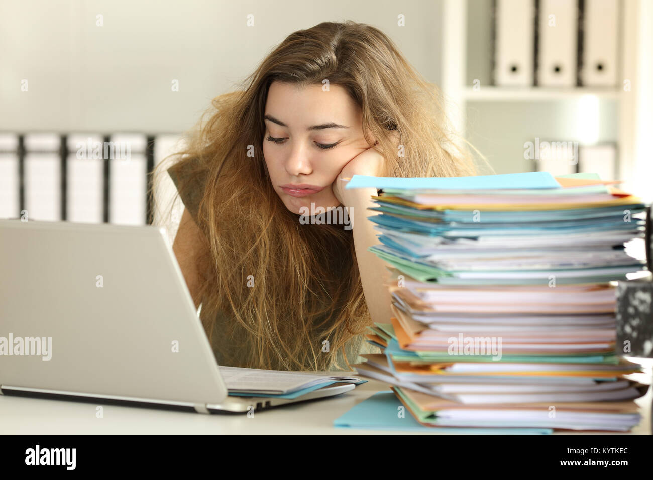 Exhausted intern with tousled hair working hard reading a lot of ...