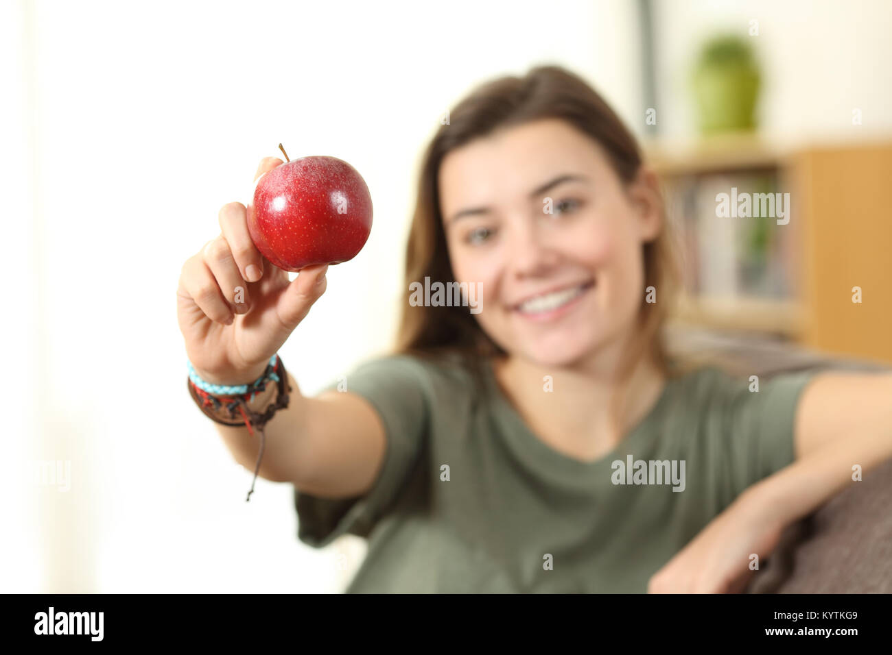Happy teenager showing an apple sitting on a couch in the living room ...