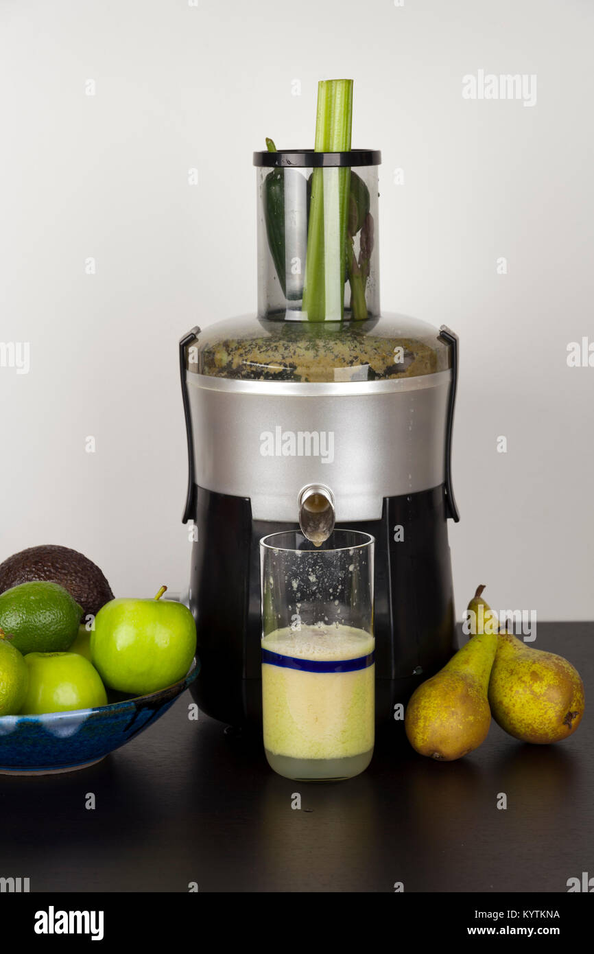 A juicer pouring fruit and vegetable juice into a drinking glass on a ...