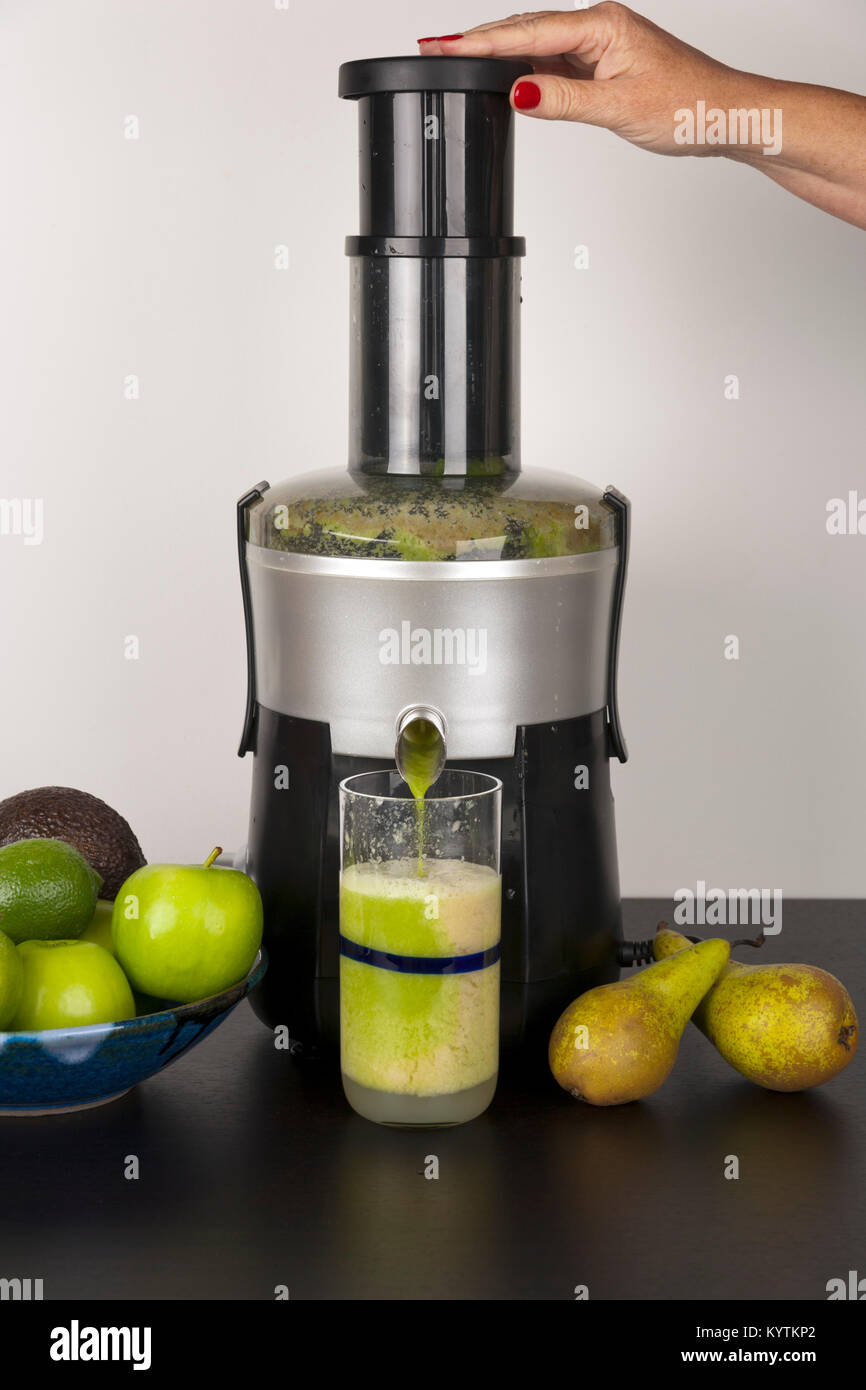 A juicer pouring fruit and vegetable juice into a drinking glass on a ...
