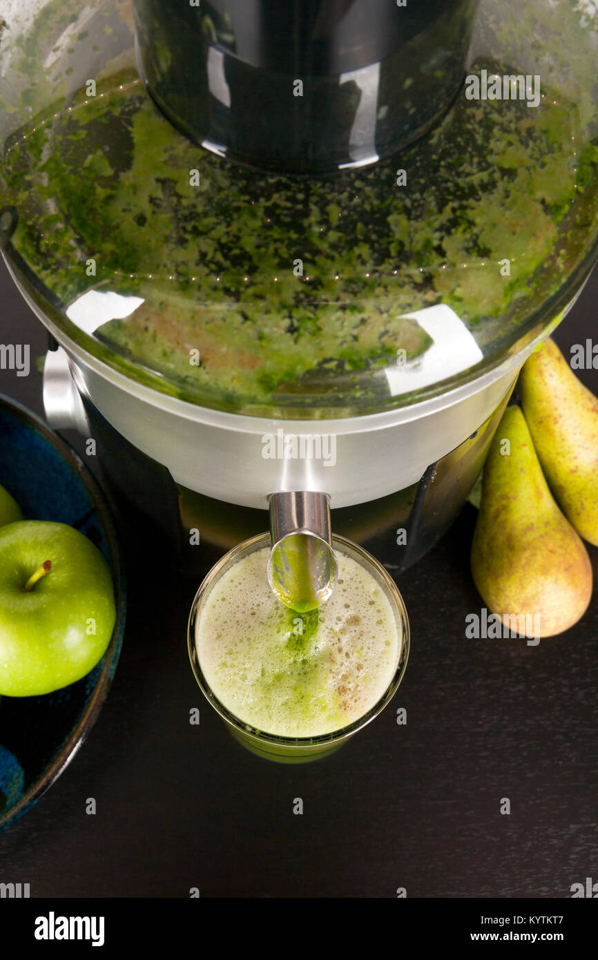 A juicer pouring fruit and vegetable juice into a drinking glass on a ...