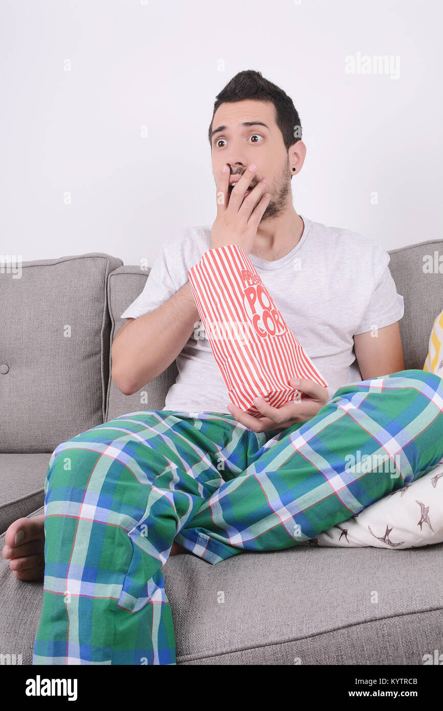 Young man eating popcorn and watching movies relaxed on couch. Indoors ...