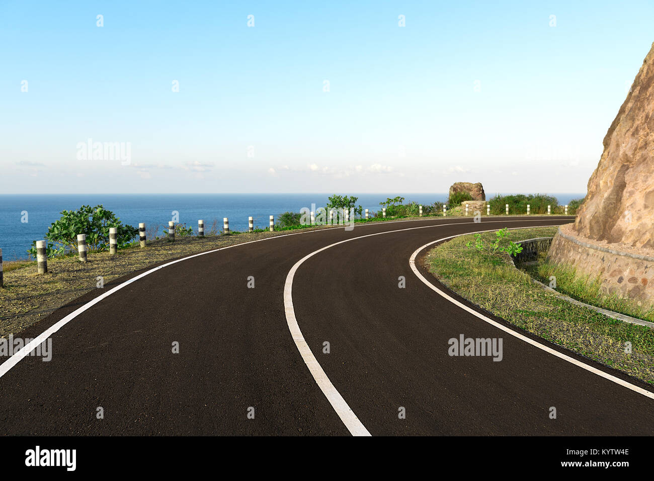 Asphalt coastal road going round cliff edge bend, with blue sea back ...