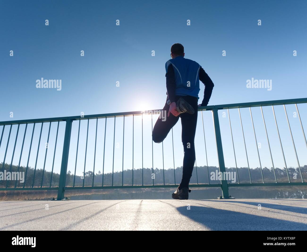The runner in tall black leggings makes body stretching on bridge path ...