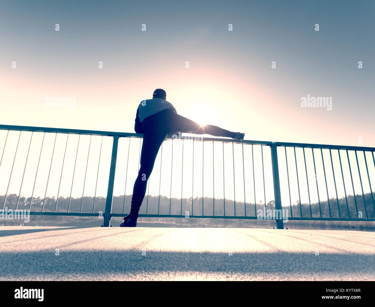 The runner in tall black leggings makes body stretching on bridge path ...
