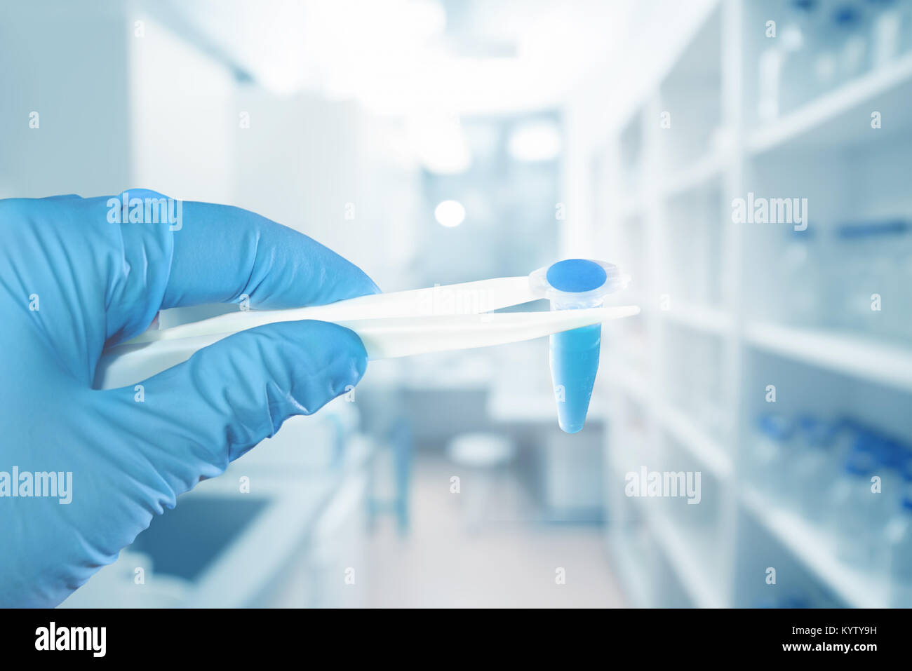 Hand in protective glove holds blue liquid sample, blurred laboratory ...