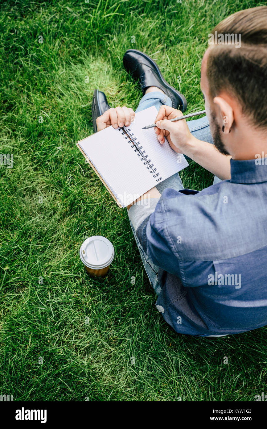 Cropped shot of man writing on notebook and drinking coffee from paper ...