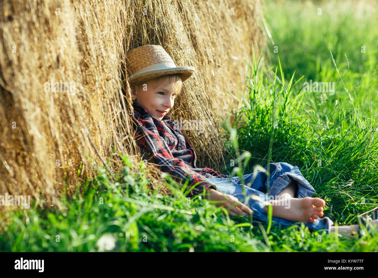 Barefooted boy in straw hat resting in haystack, outdoors, side view ...