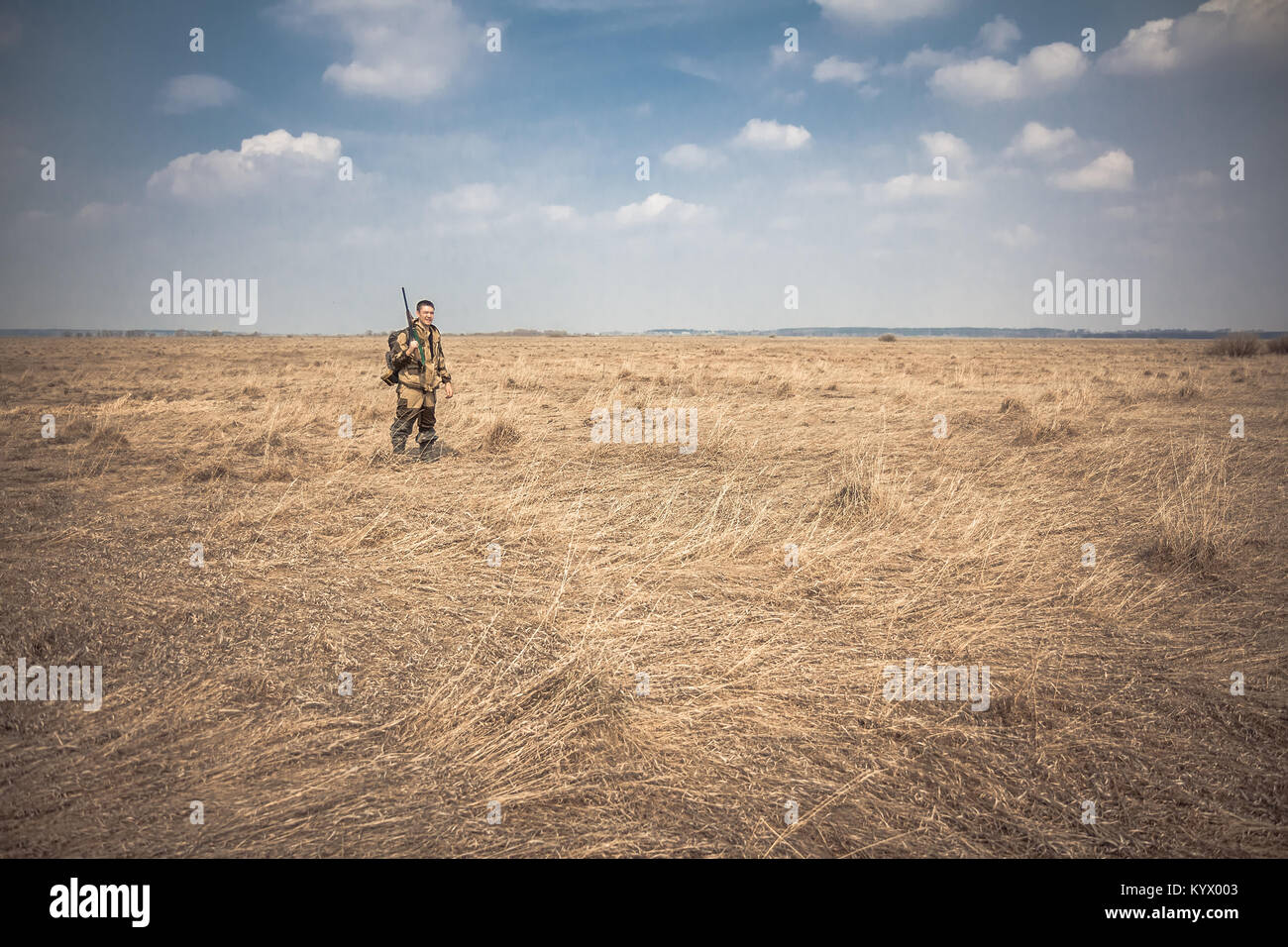 Hunter man with shotgun and hunting equipment standing in dry rural ...