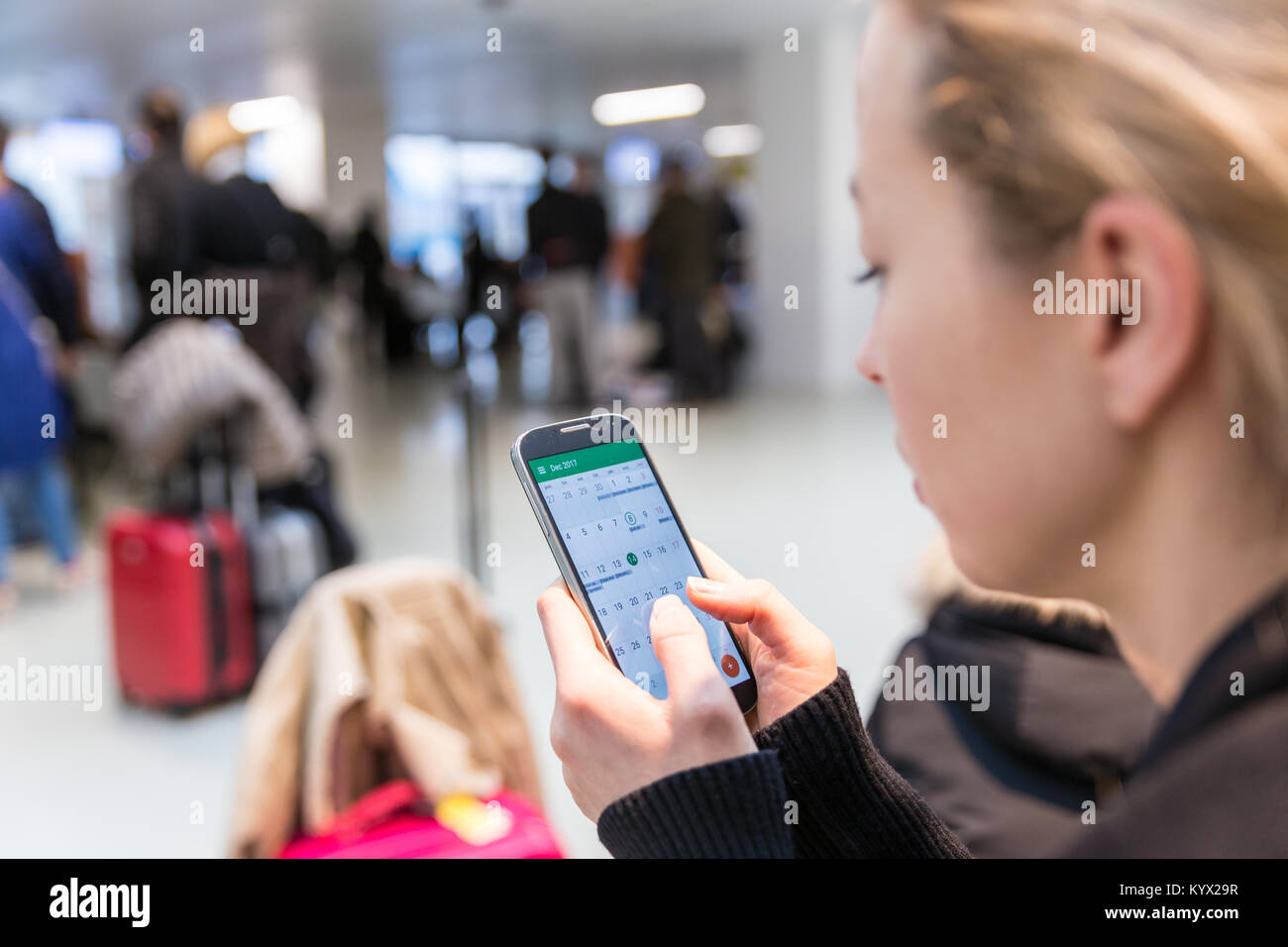 Woman checking information on mobile phone sitting in airport terminal ...