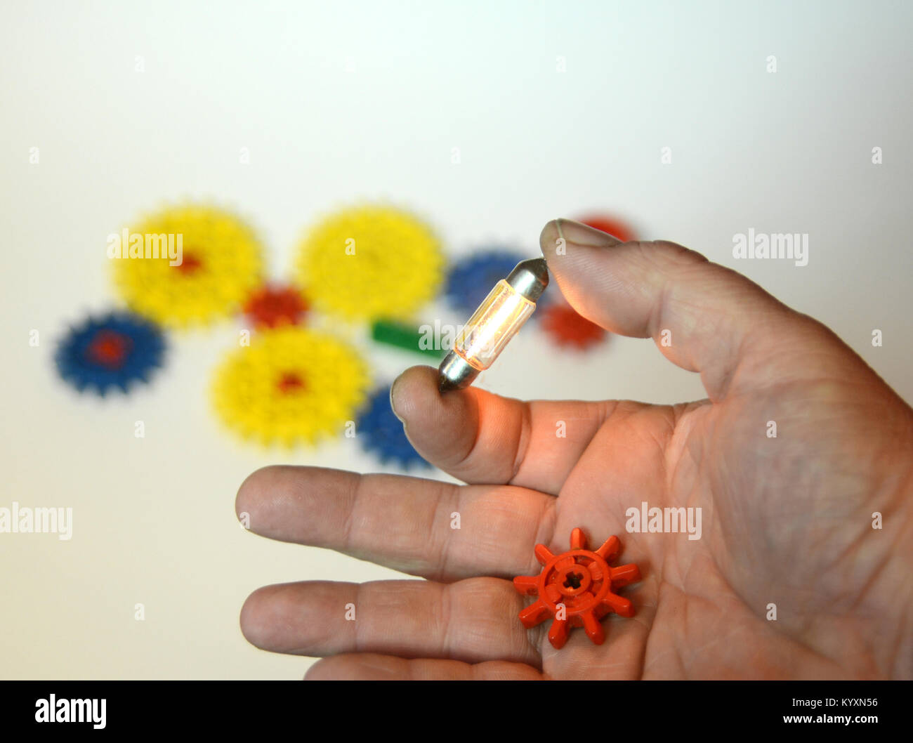 Hand holds light bulb with light and cogwheel, more colored unsharp ...