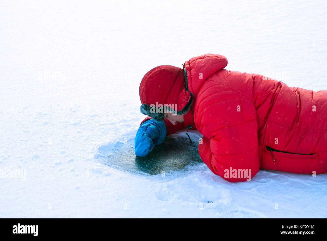 a man in winter lies on the surface of a frozen river and looks under ...